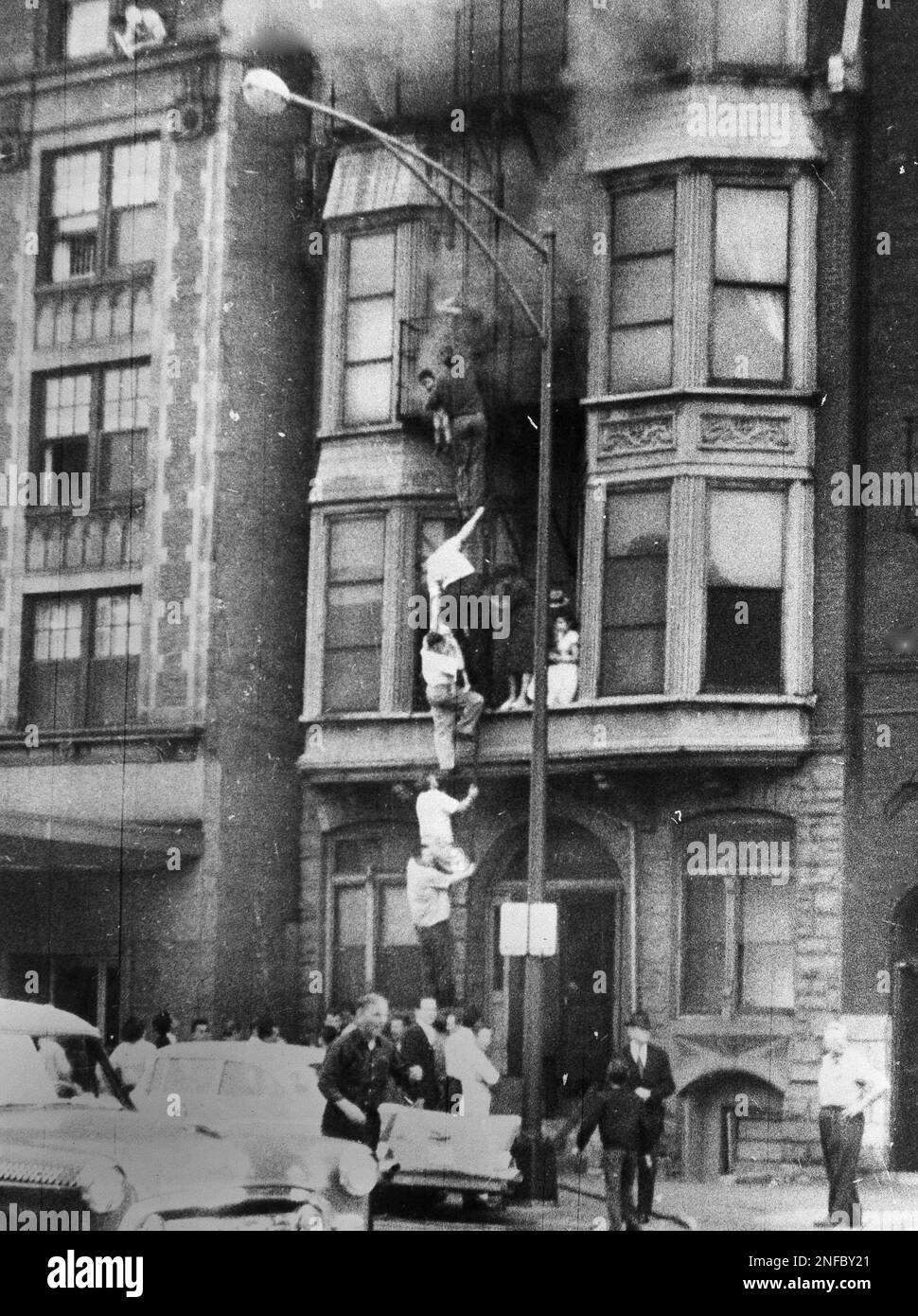 A chain of people fleeing a fire descends a ladder fire escape as smoke ...