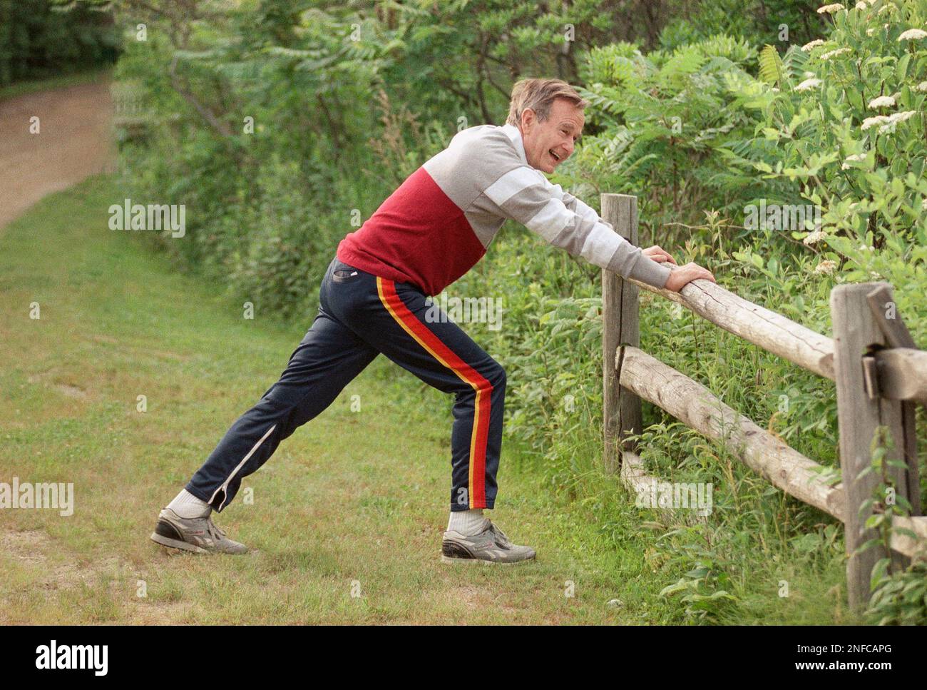 President George Bush stretches on a fence rail before jogging near his ...
