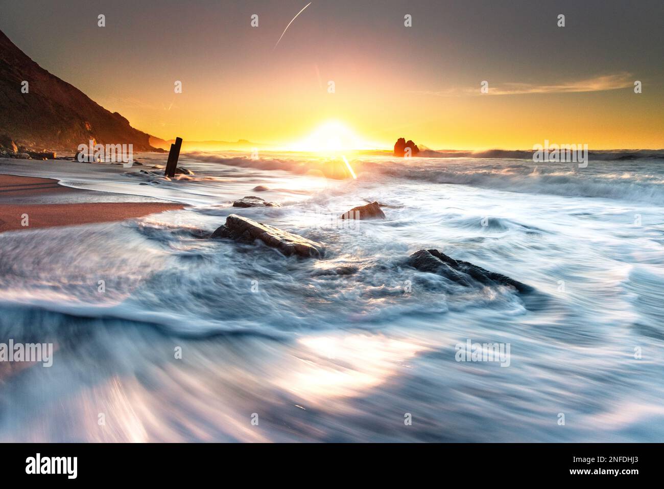 Sunset while sea waves hitting the rocks on the beach; at Ilbarritz ...