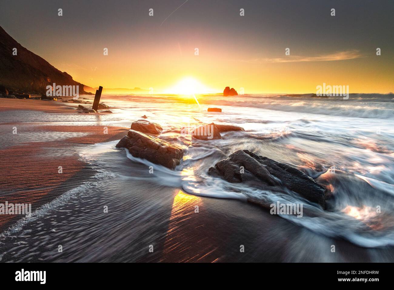 Sunset while sea waves hitting the rocks on the beach; at Ilbarritz ...