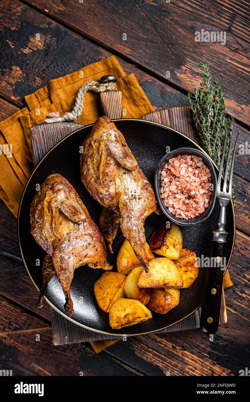 Roast whole quails in a plate with fried potato. Wooden background. Top ...
