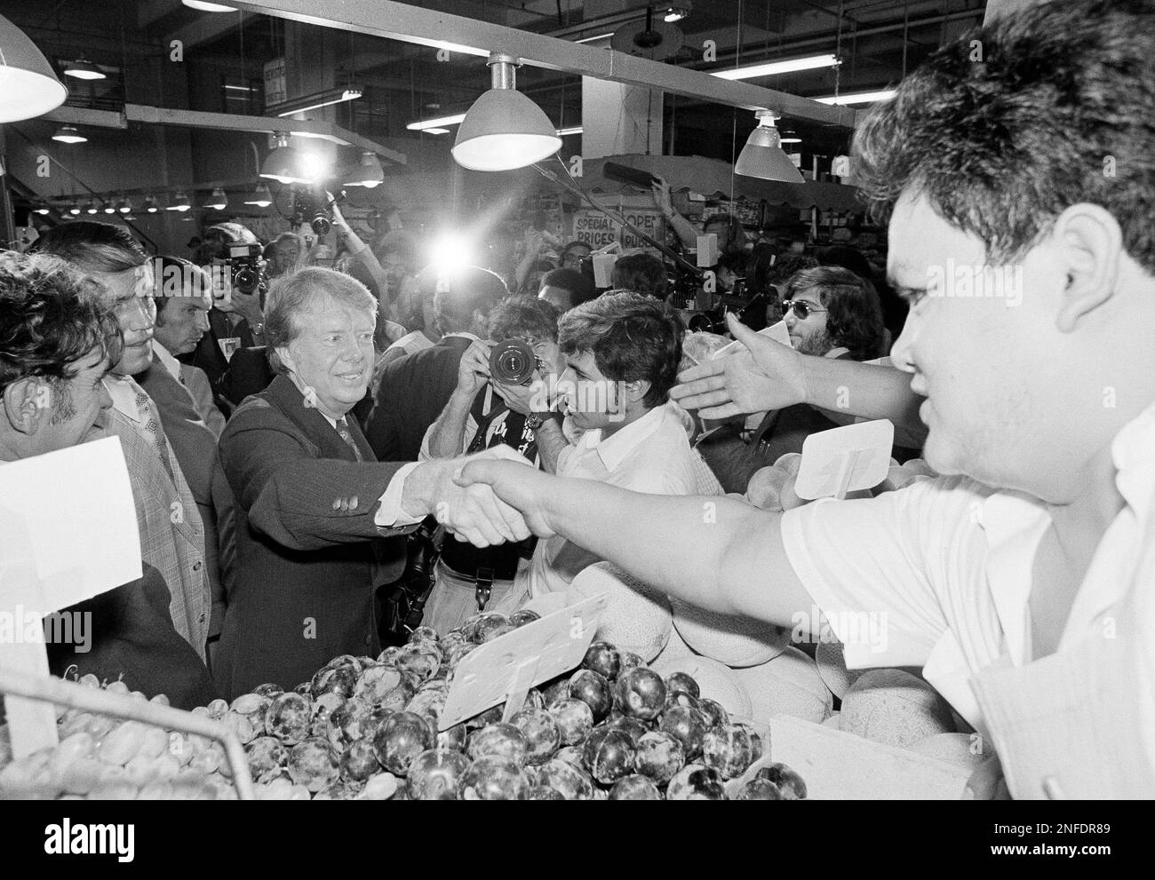 Jimmy Carter reaches across a counter full of fruit to shake hands with ...
