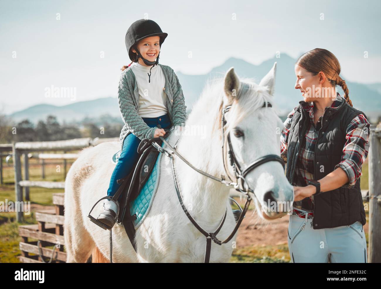 .Happy child on horse, woman with harness on ranch and mountain in ...