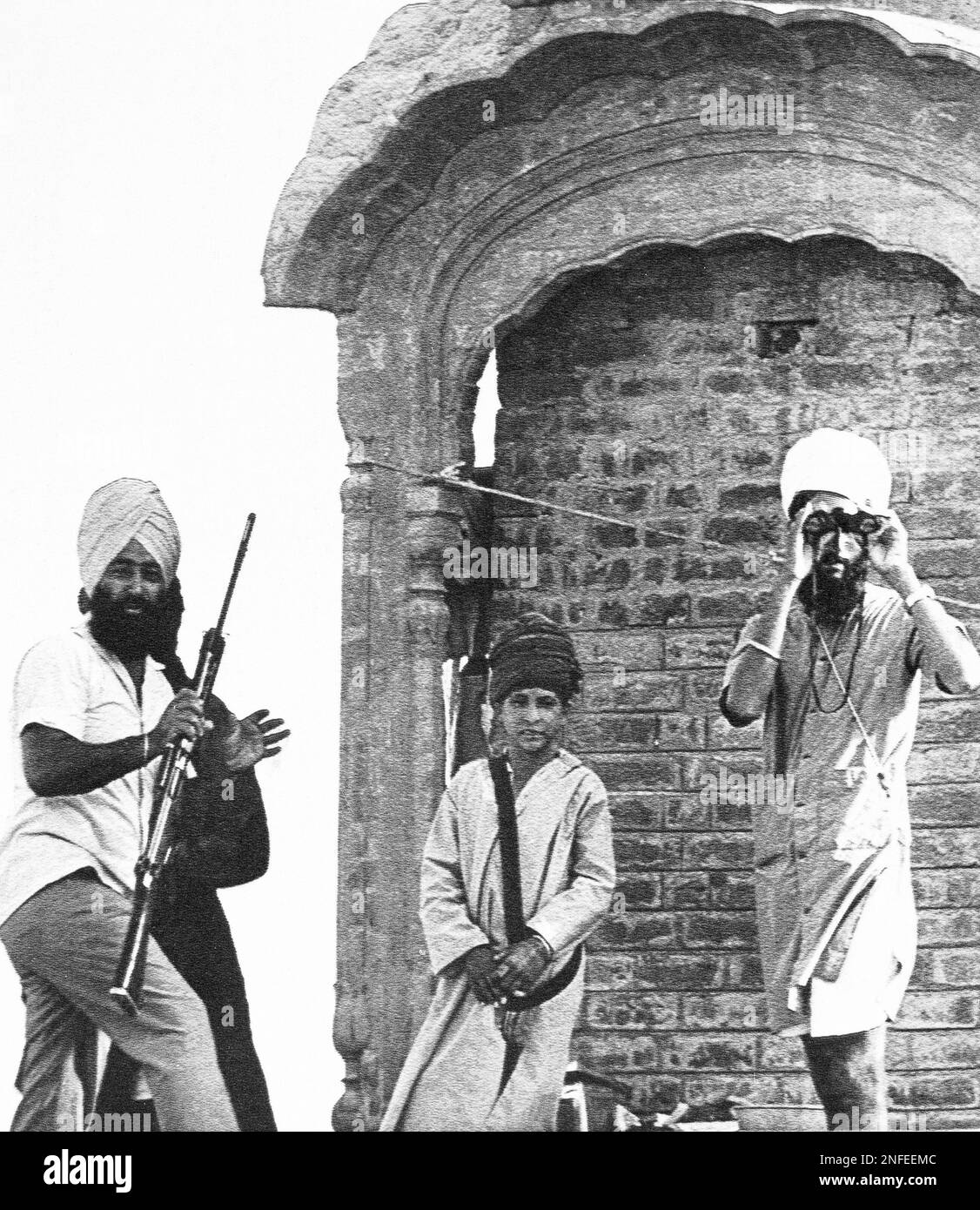A Sikh militant holds field glasses to look at government troops from ...