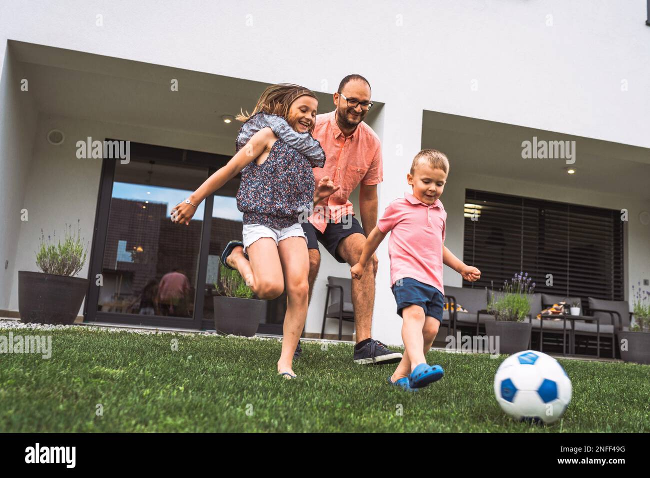 Father and his two children running after a football rolling down the ...