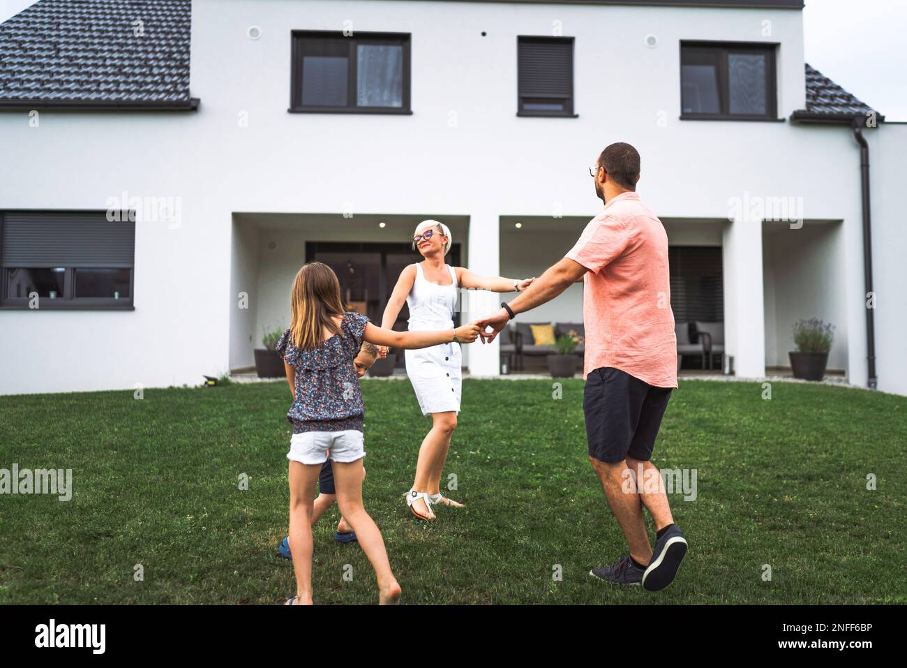 Family dancing together on the grass outside in circle, their new built ...