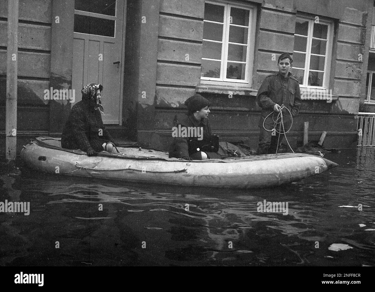 A young man pulls two women a dinghy through the flooded streets of ...
