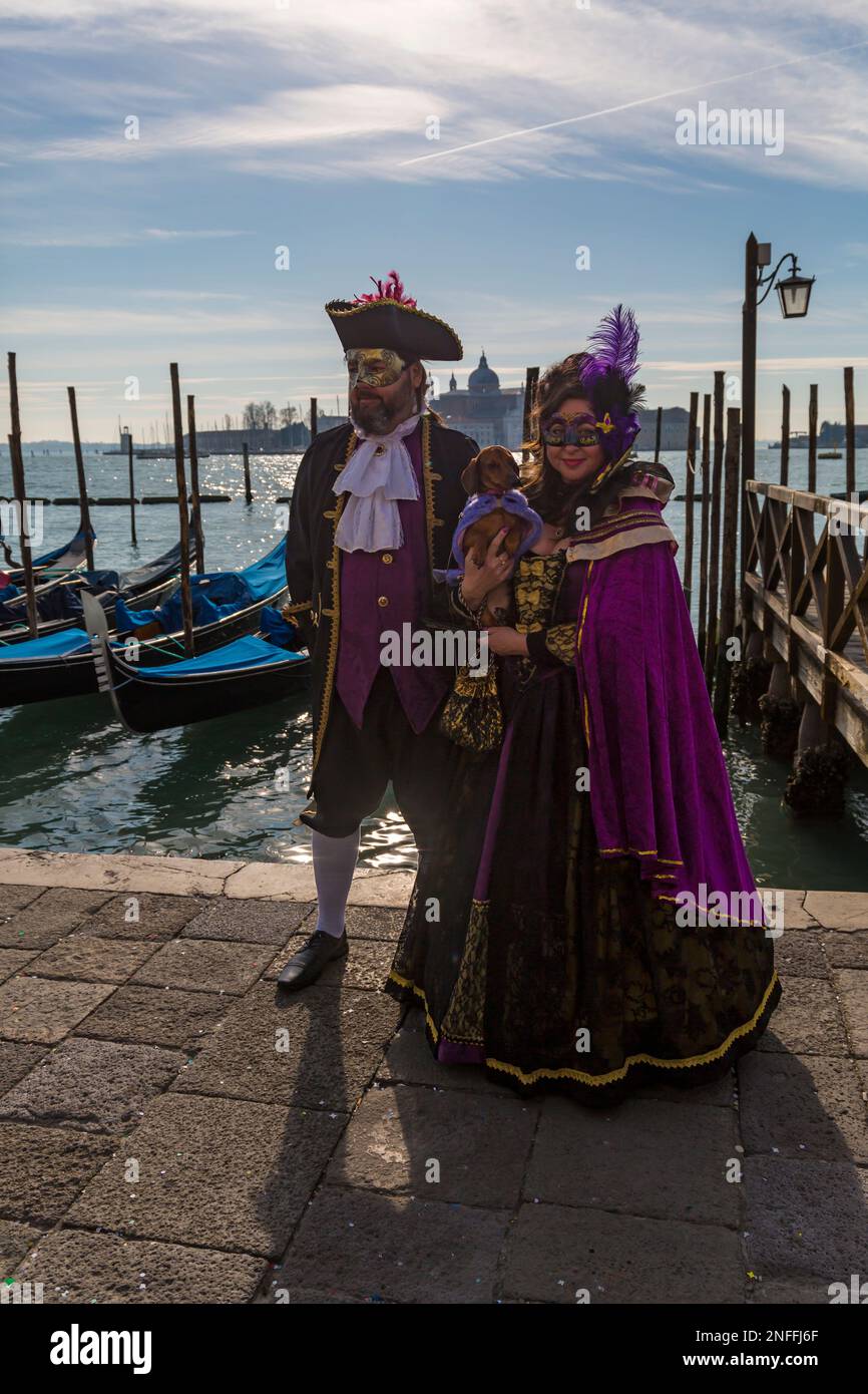 Carnival goers dressed in splendid costumes and mask holding dog during ...