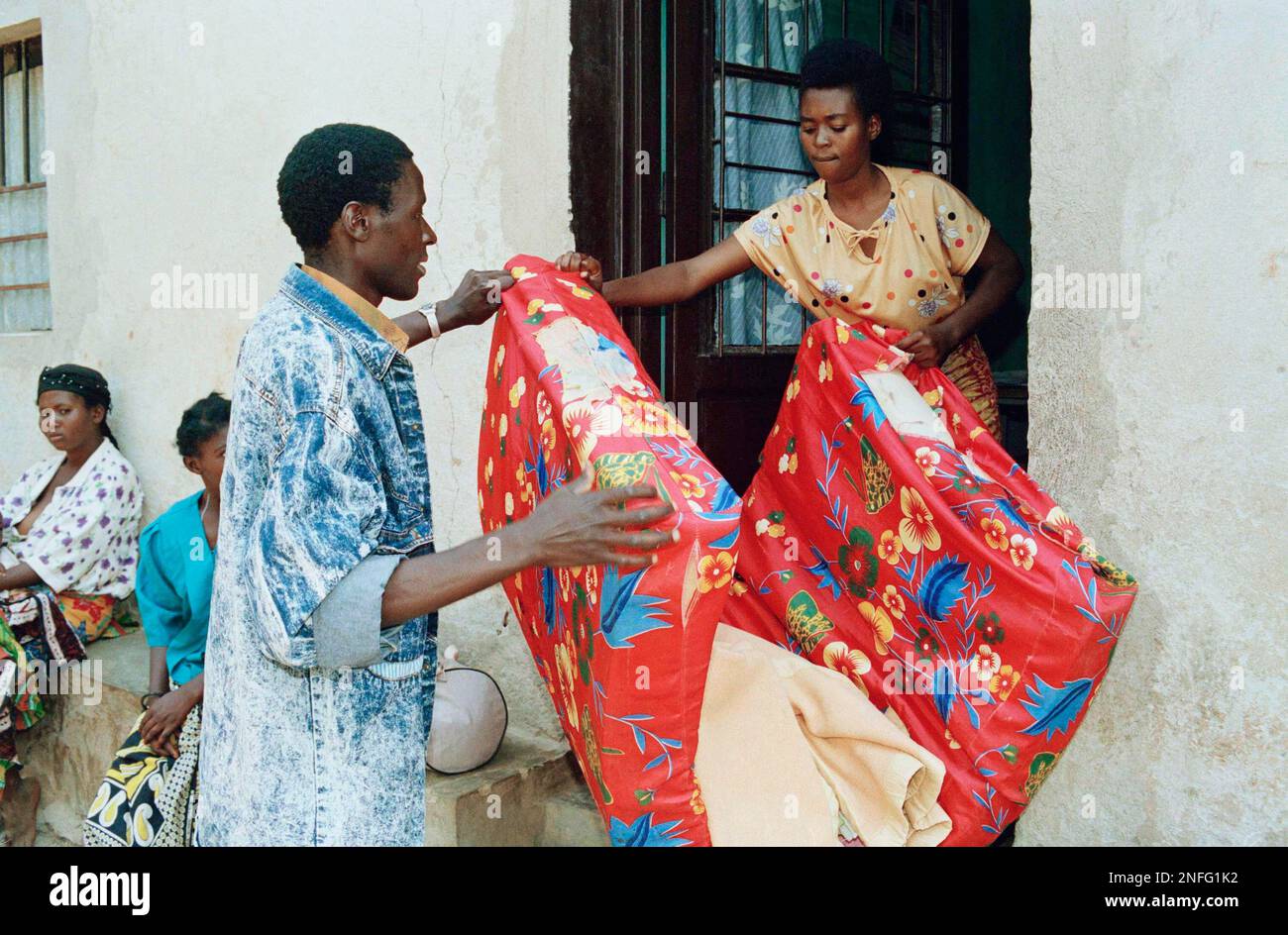 A Rwandan man assists his sister in law as the family moves back into ...