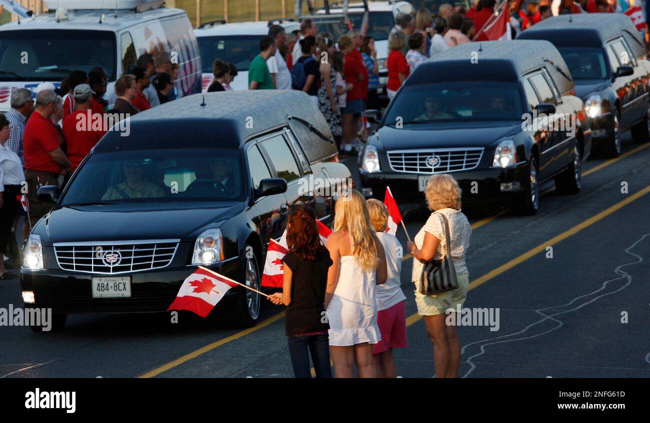 Members of the public watch as a motorcade of hearses carry the caskets ...