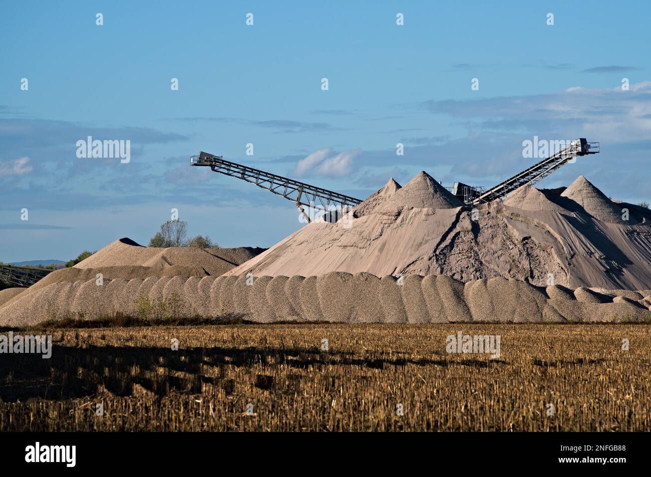 Heaps of sand near a gravel plant with two conveyor in the evening sun ...
