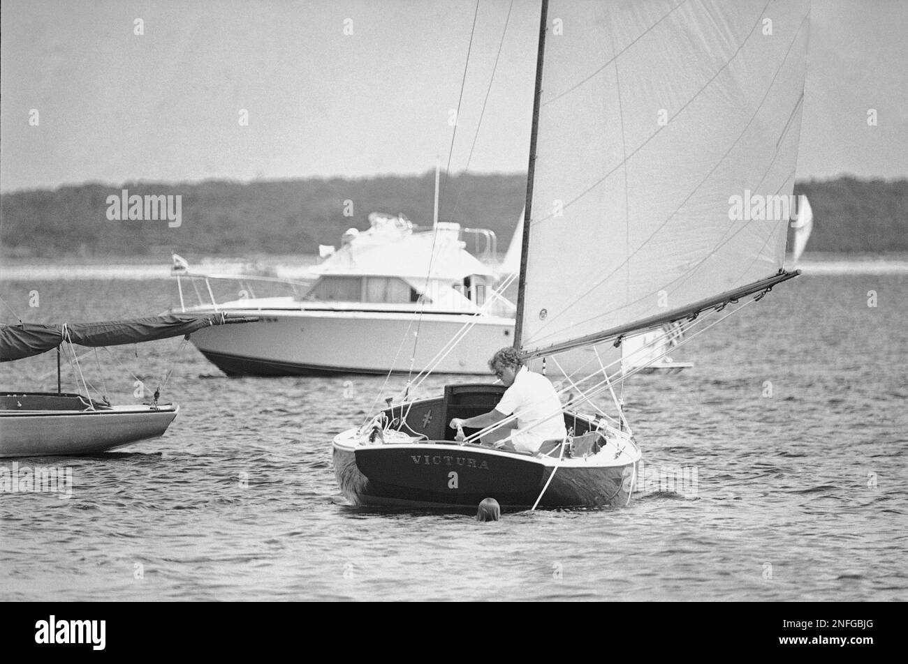 Sen. Edward M. Kennedy mans the helm of a small sailboat as he tows an ...