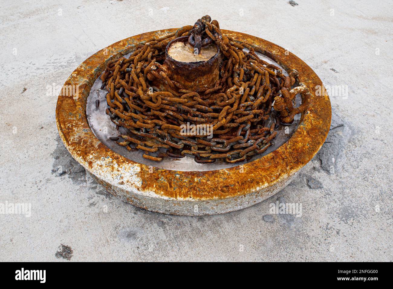 Rusted metal chain coiled around base on a light gray stone dock at a ...