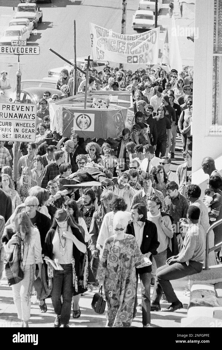 Hippies carry a box-like coffin and a hippie on a stretcher through ...