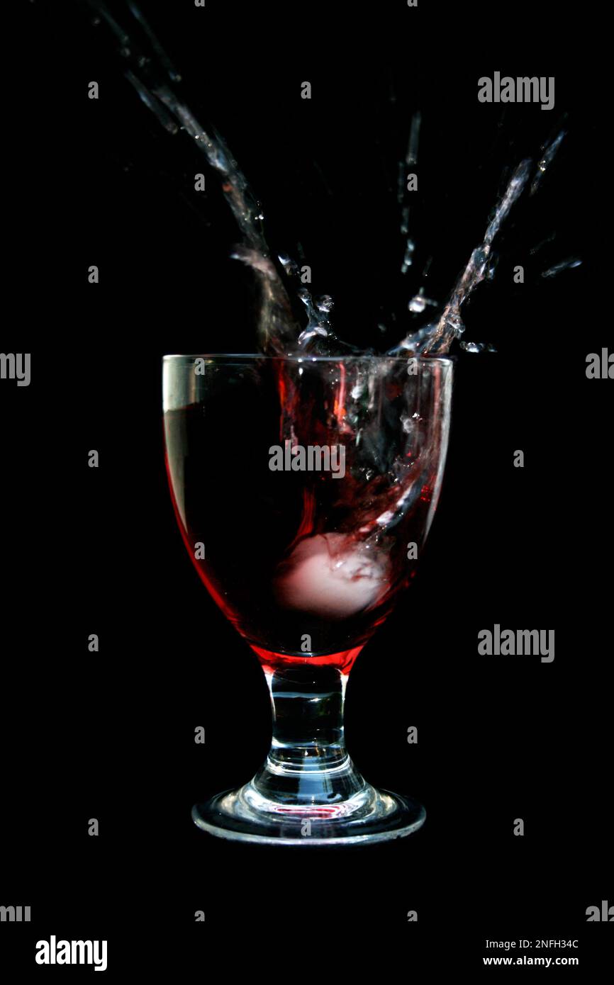 Freezing motion of an ice cube splashing in a glass against a black ...