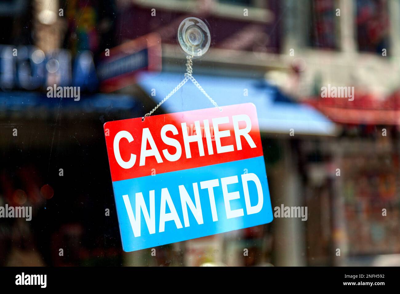 Red and blue sign in the window of a shop saying "Cashier wanted Stock ...