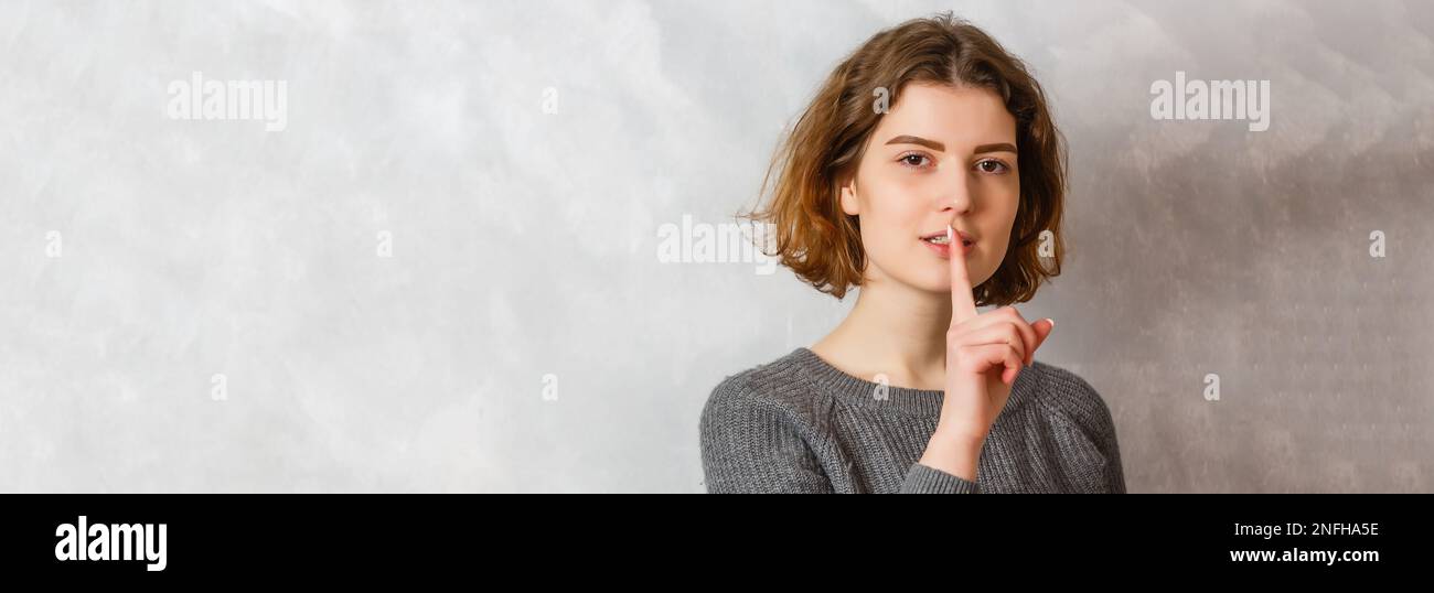 Pretty girl making silence gesture over grey background Stock Photo - Alamy