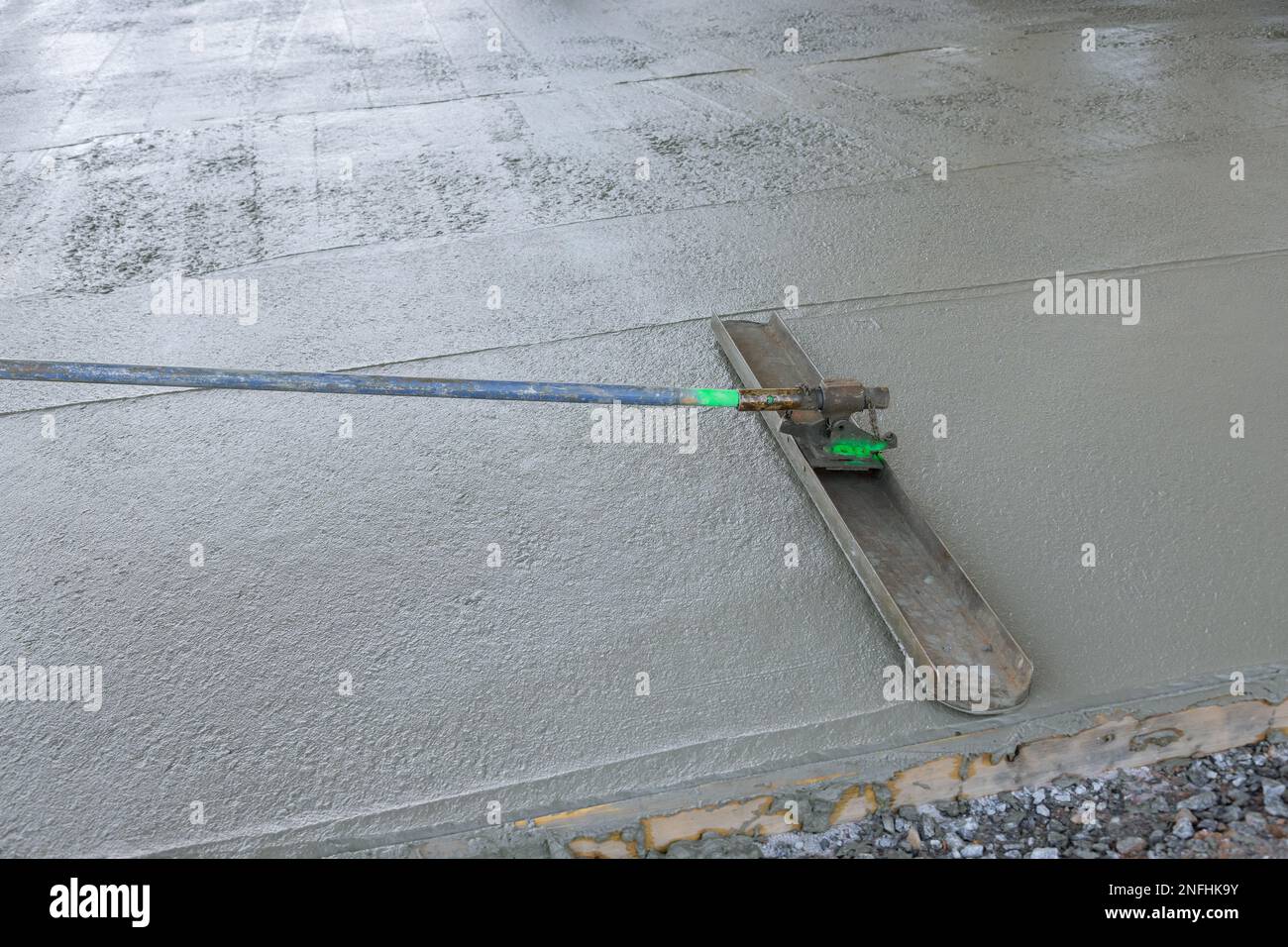On wet cement sidewalk construction worker use long trowel to level ...