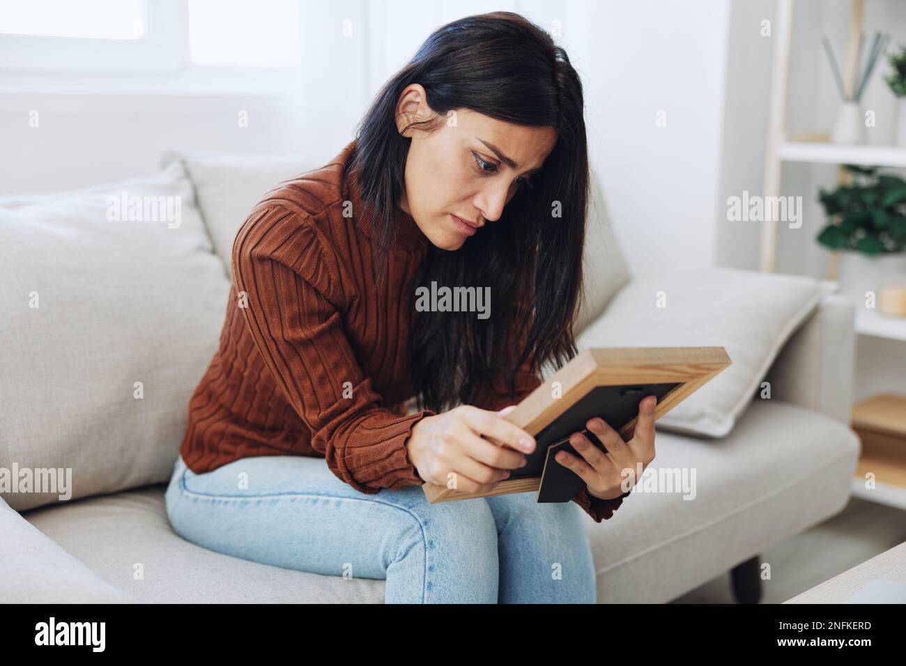 Woman looking sadly at the picture frames in her hands, crying over ...