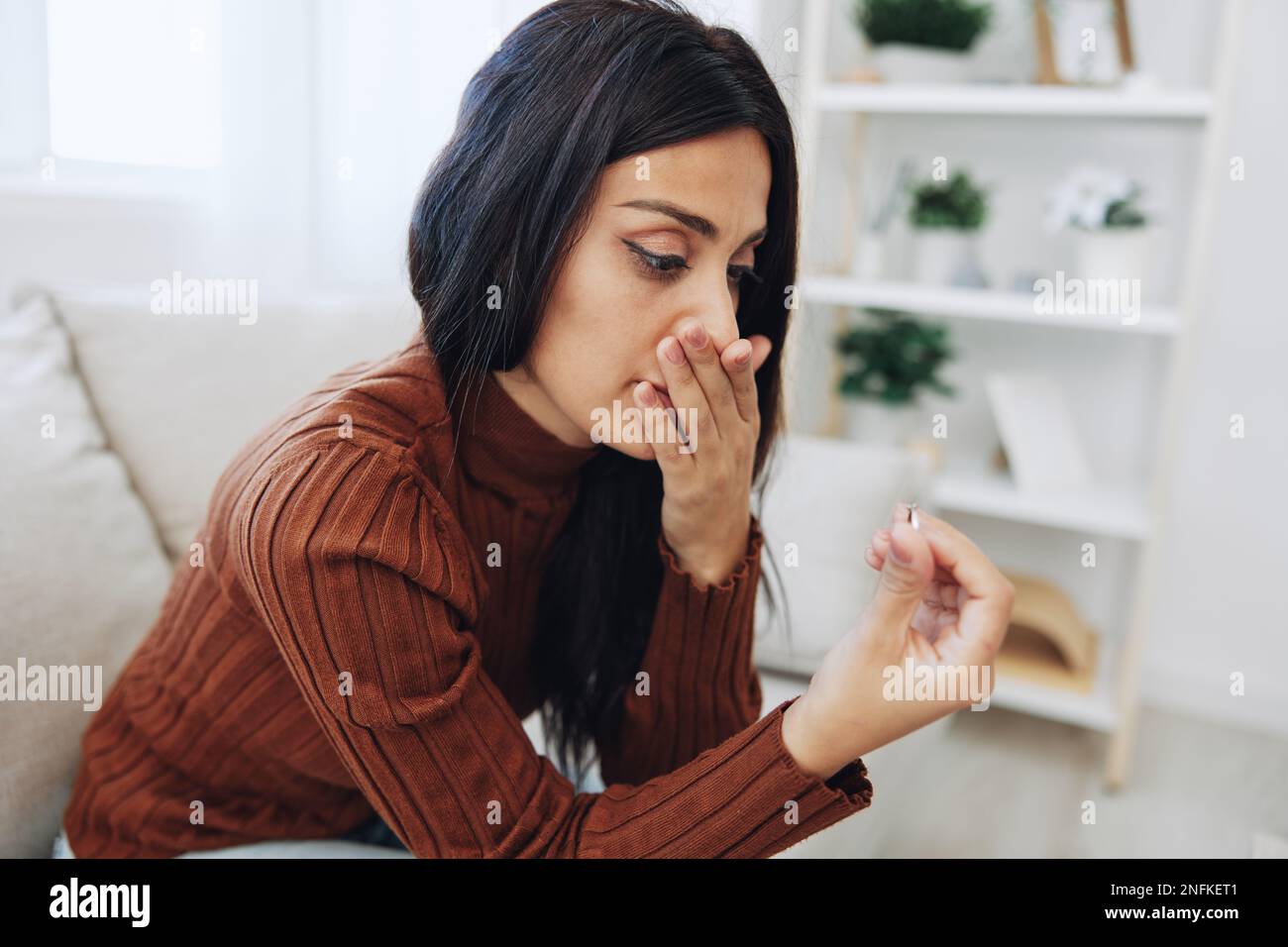 A woman looks sadly at a wedding ring in her hand, divorce and loss of ...