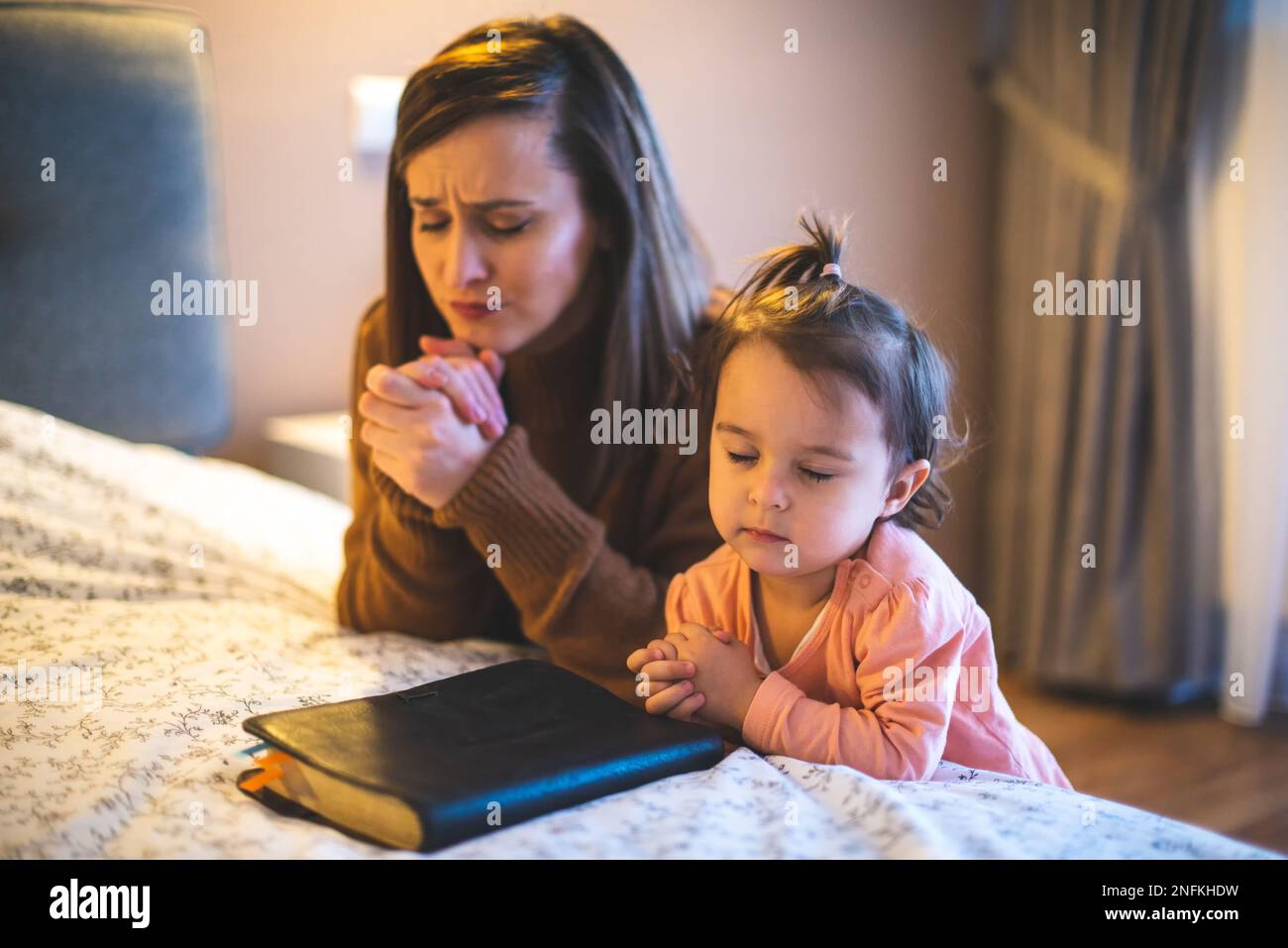 mother and her little girl praying at the edge of the bed in the ...