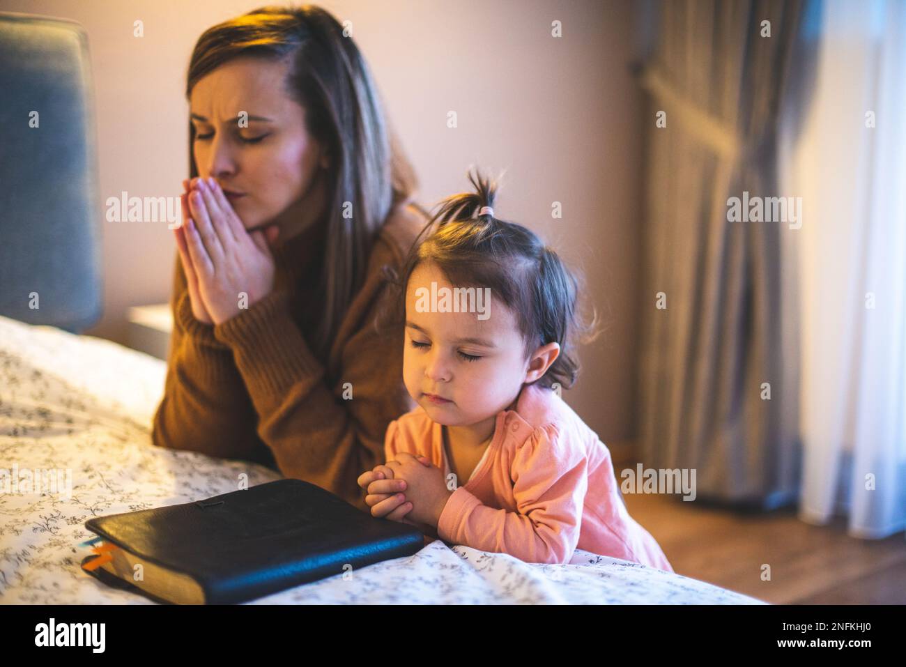 Mother and her daughter reading from bible and praying in their knees near the bed Stock Photo ...