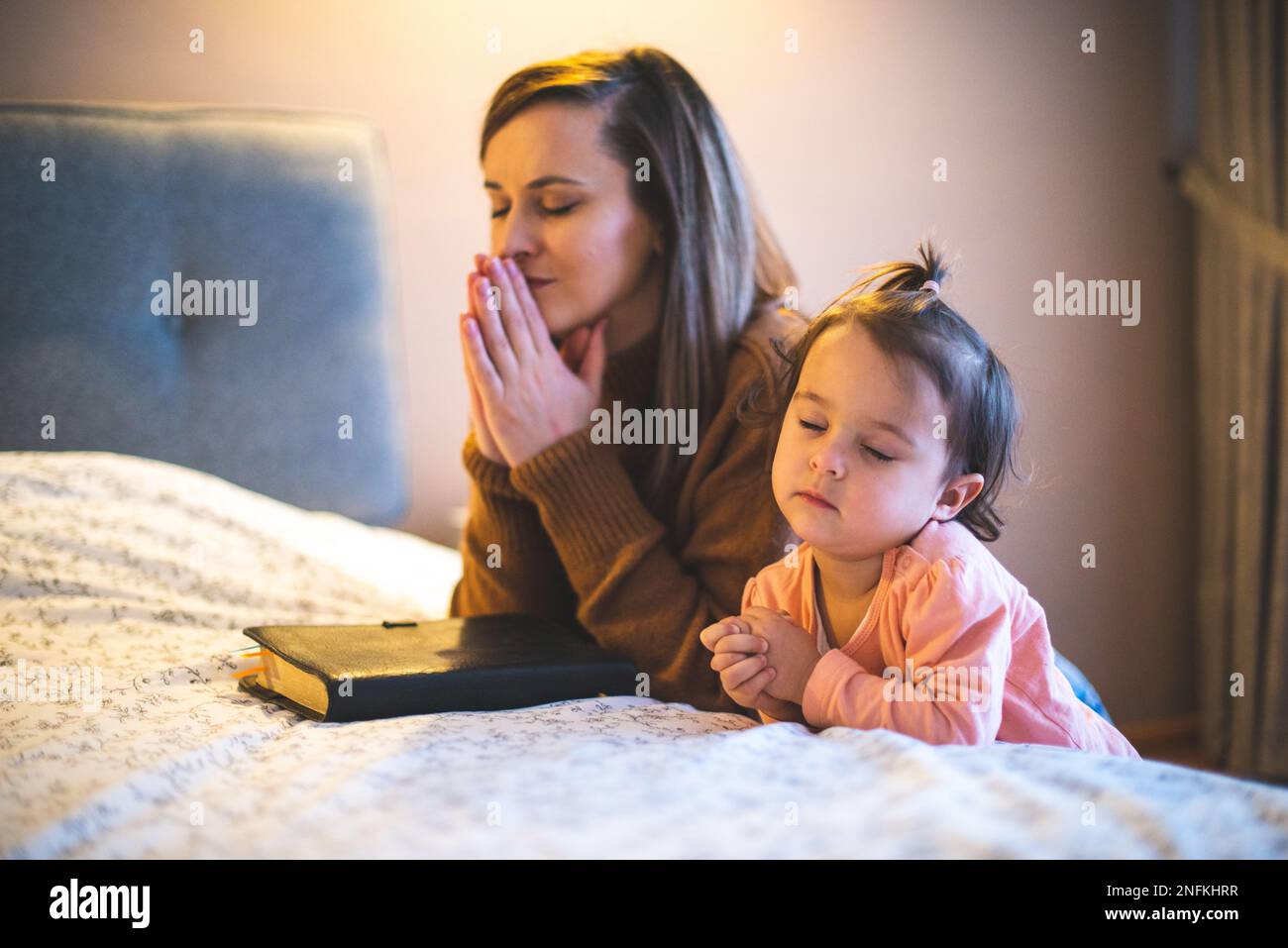 Mother and her daughter reading from bible and praying in their knees near the bed Stock Photo ...