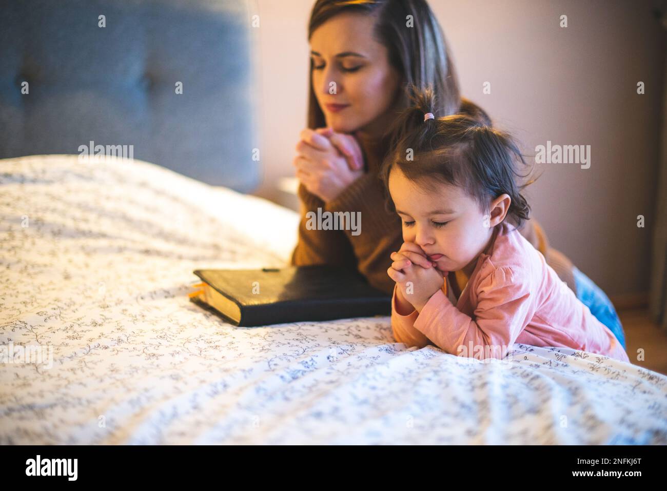 Mother and her daughter reading from bible and praying in their knees ...
