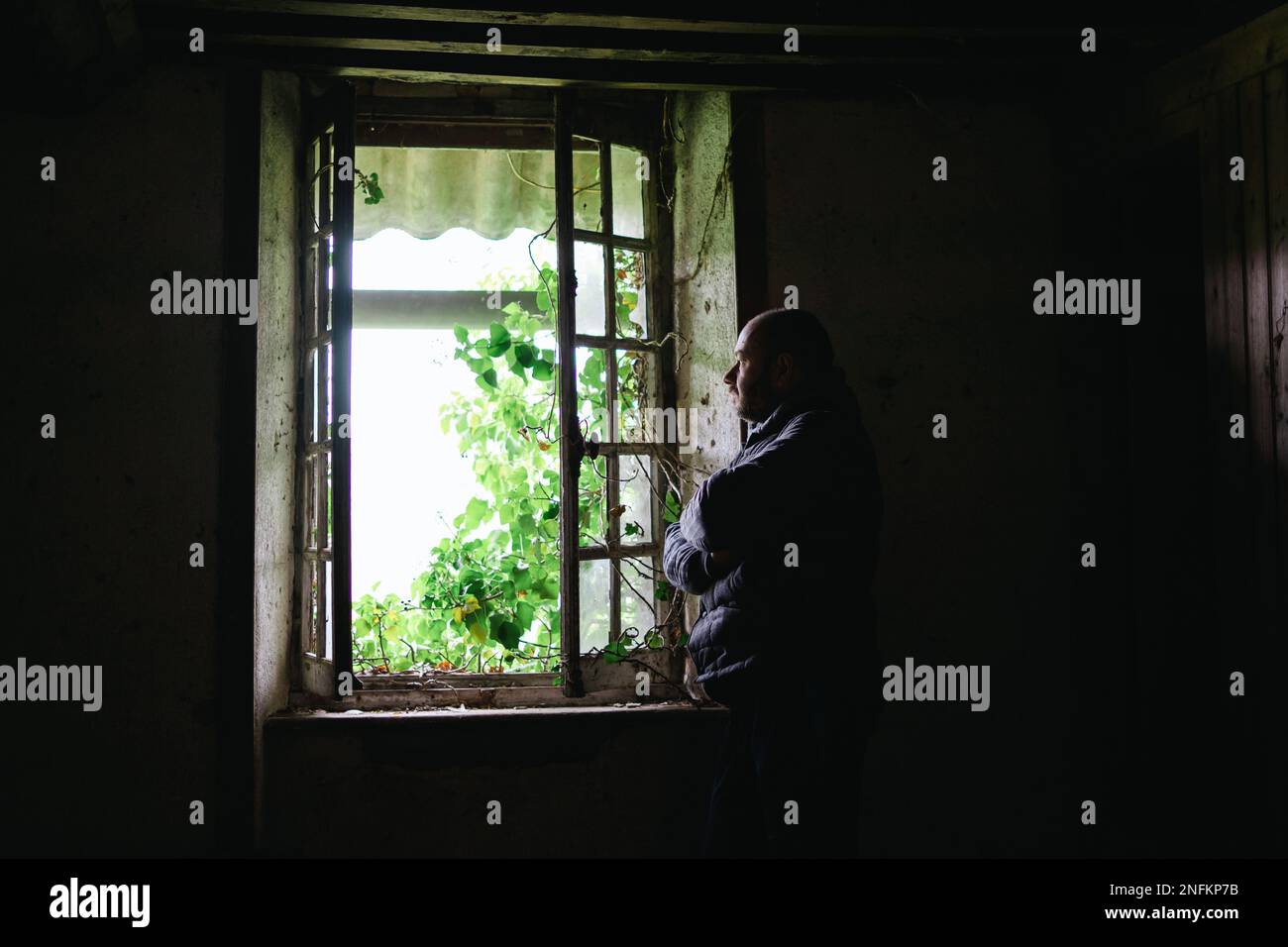 A man inside an old crumbling house near the window. Depression ...
