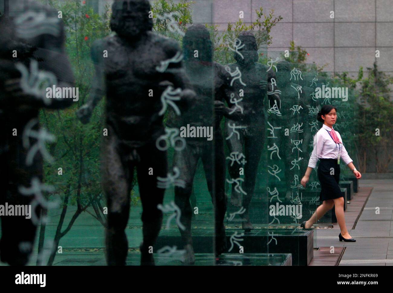 A Chinese hostess walks past sculptures of runners at the Olympic Green ...