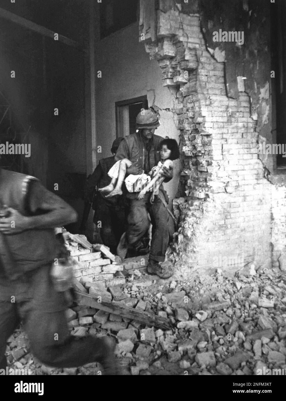 A Marine carries a seriously wounded child from the ruins of a house in ...