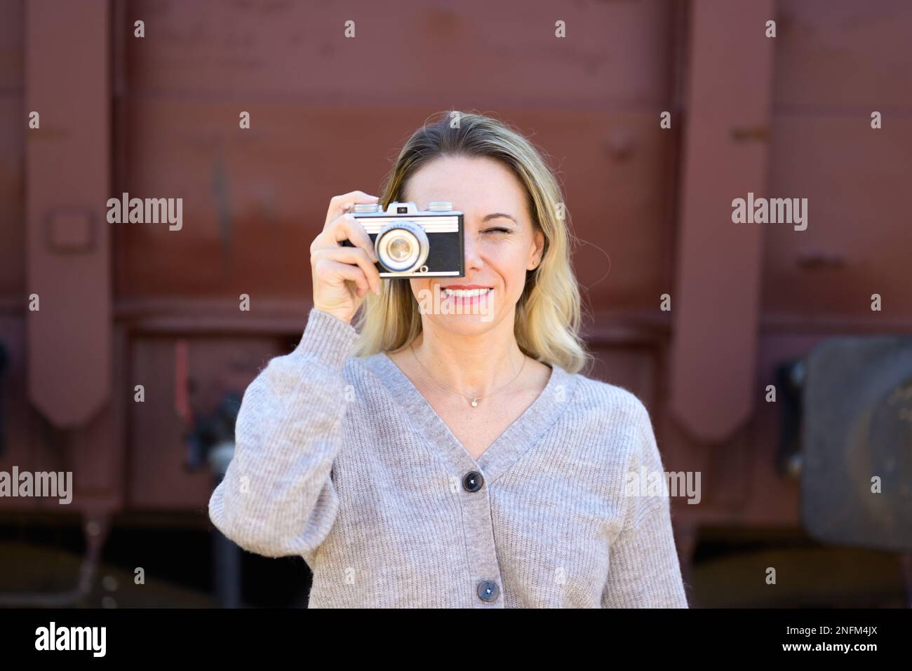 Smiling middle aged woman with an old camera is taking a picture and ...