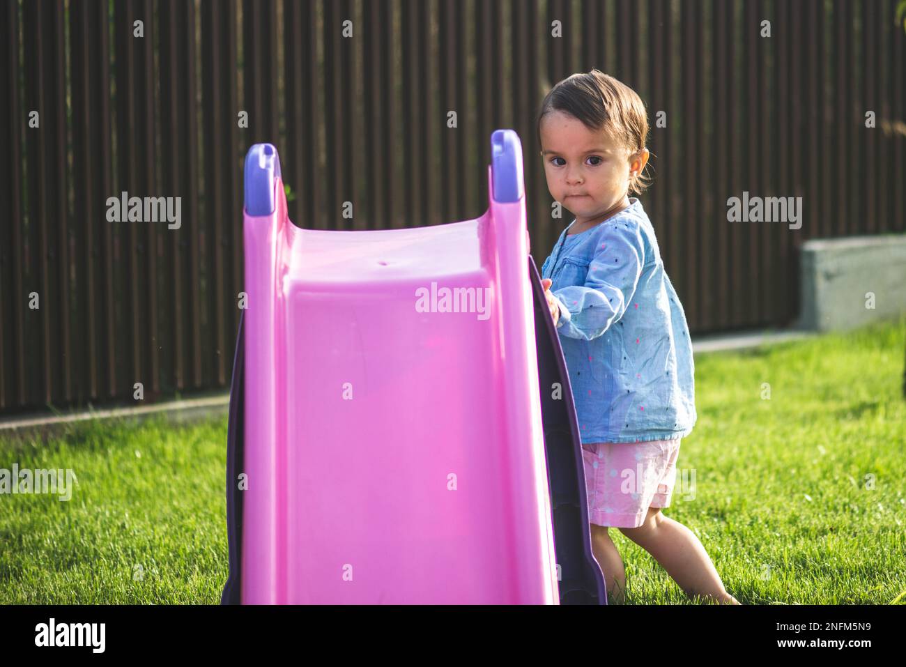 Little and cute girl play on slide and make a grimace while she play ...