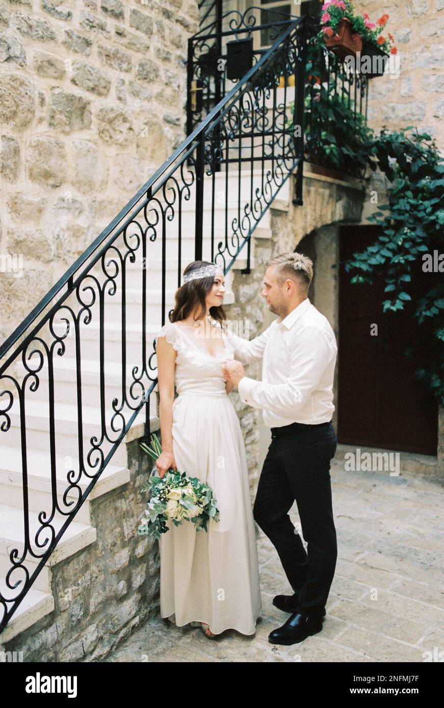 Bride and groom are standing near the stairs of an old stone house ...