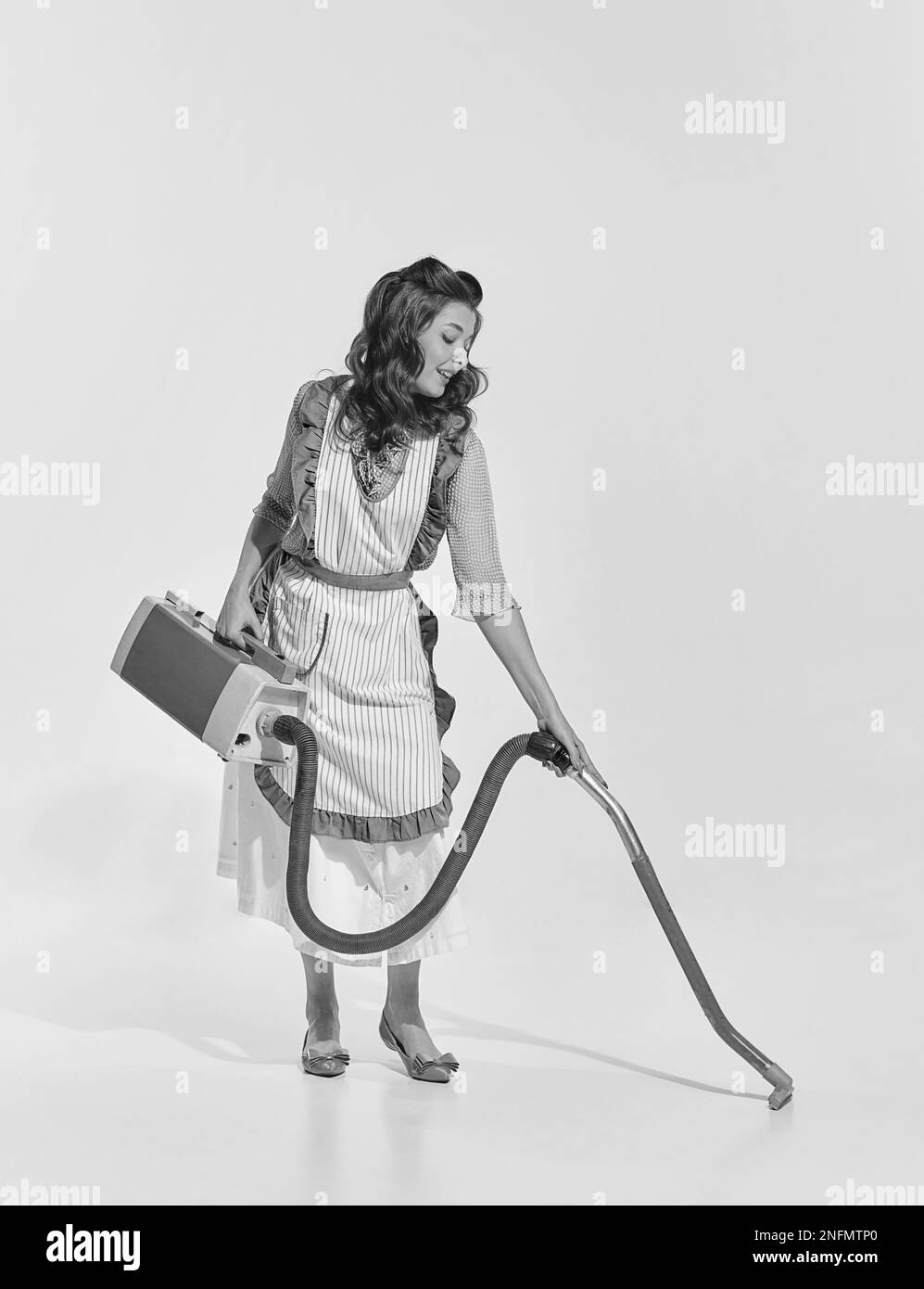 Portrait of young beautiful retro woman cleaning house with vacuum ...