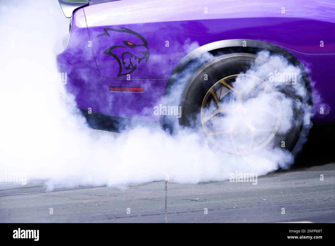 A close-up of a purple car driving through the smoke with black rims ...