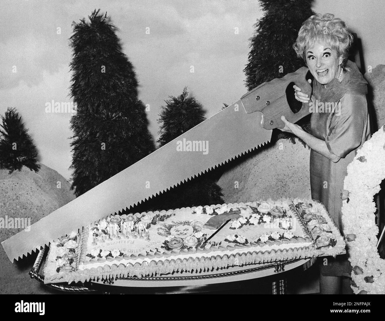 Phyllis Diller hefts a man-sized saw to cut her birthday cake at a ...
