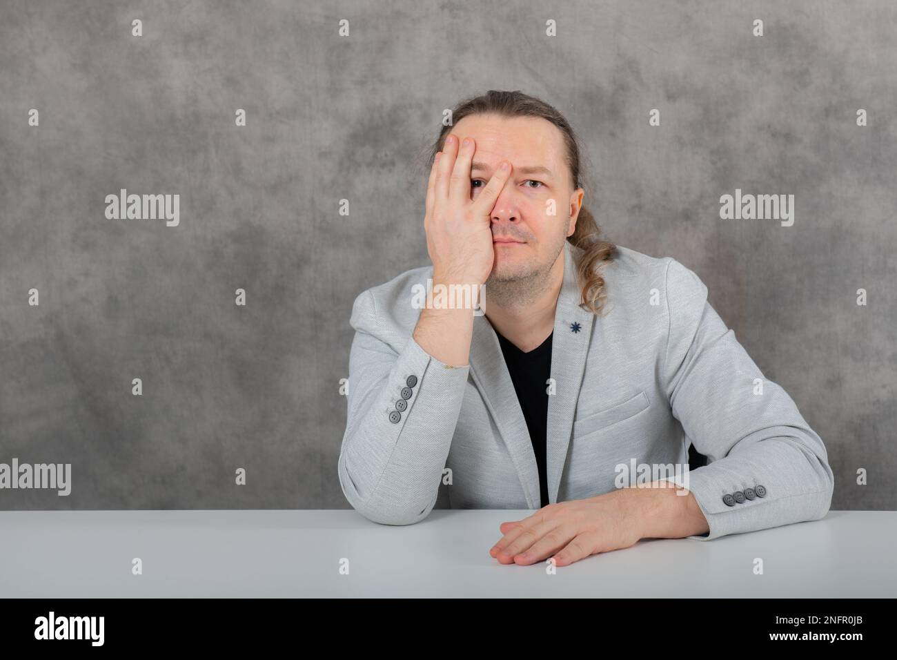 One man in a gray suit covers his face with one hand Stock Photo - Alamy