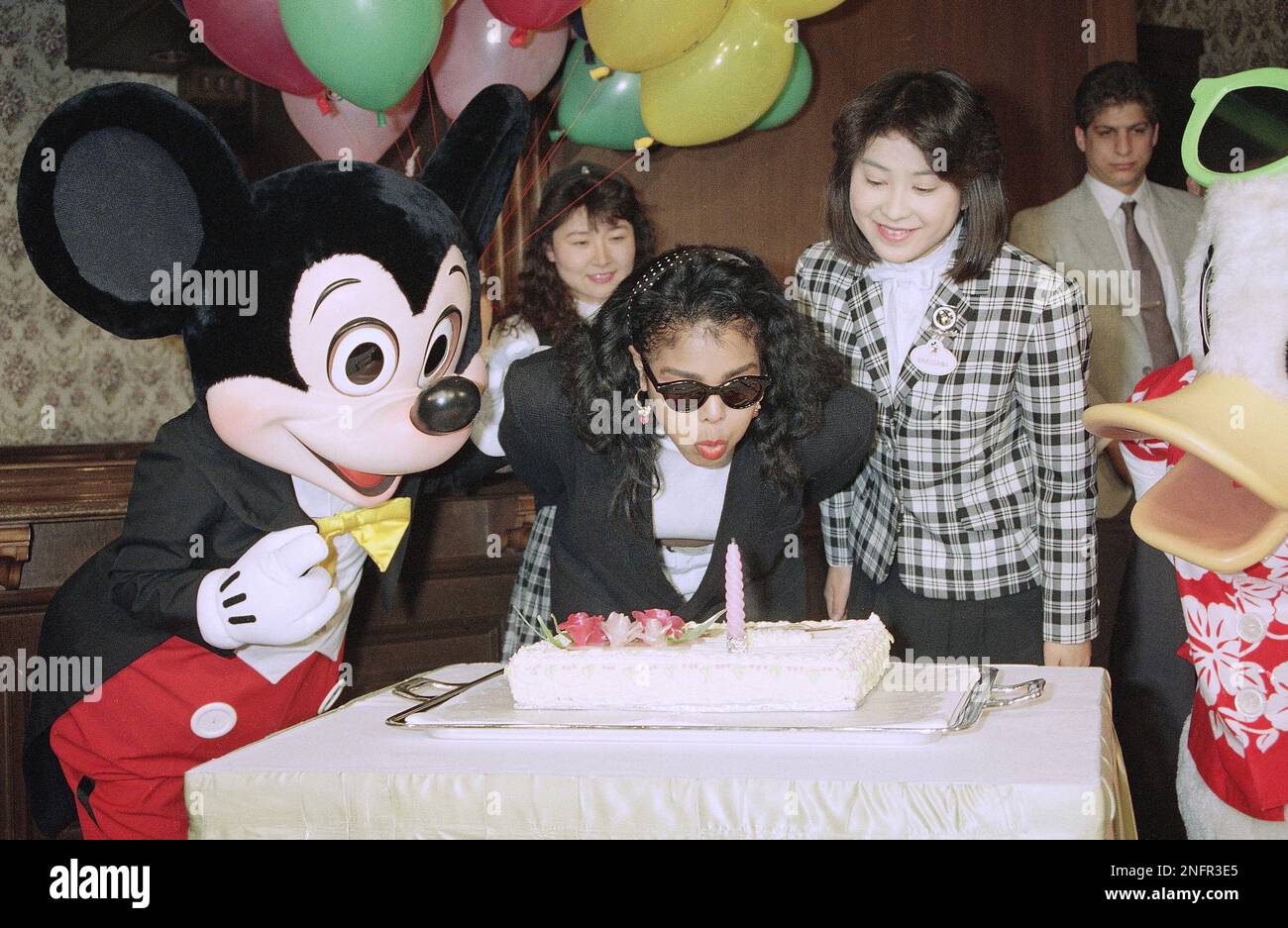 Flanked by Mickey Mouse, singer Janet Jackson blows out the candle on ...