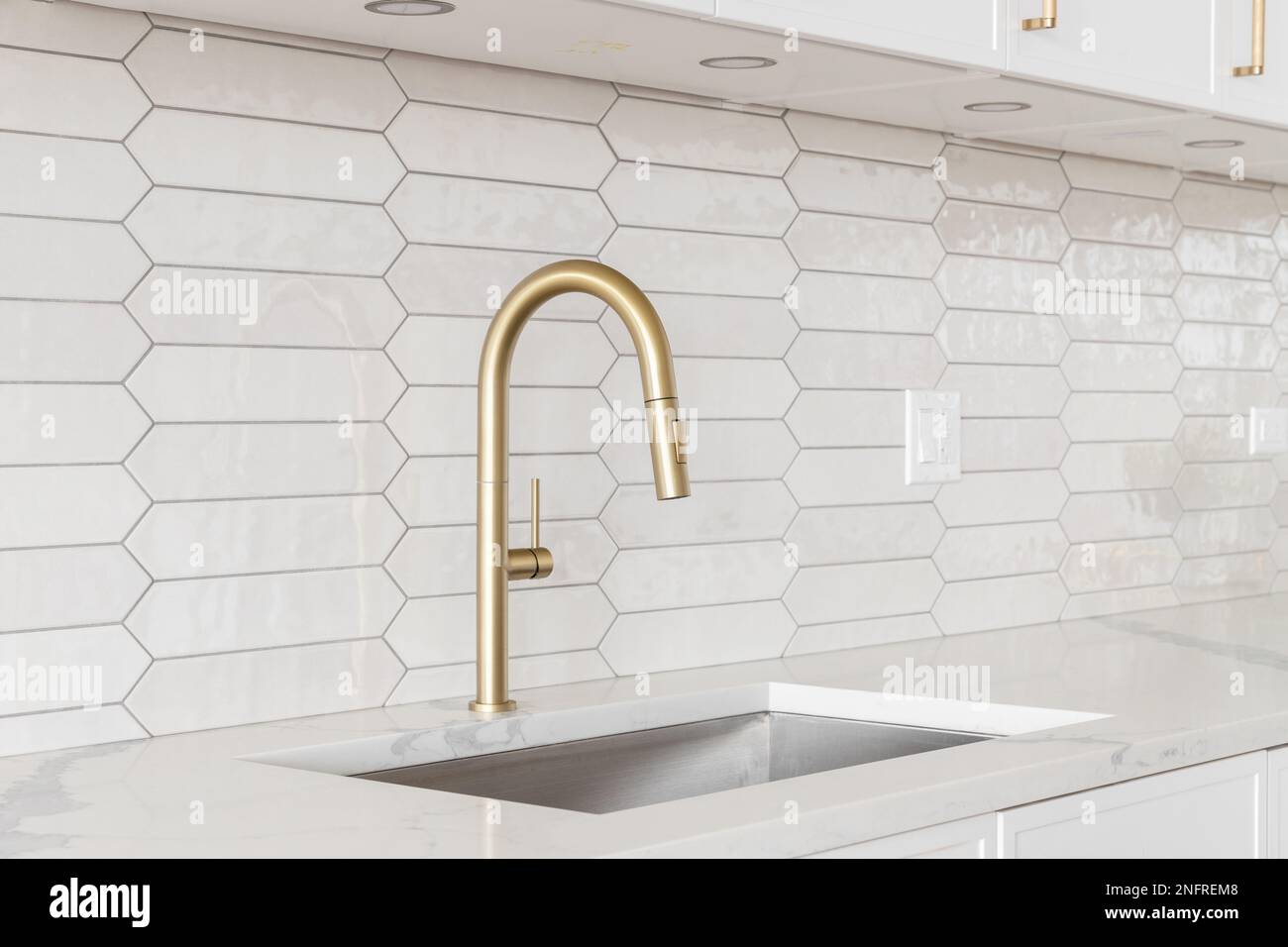 A beautiful kitchen faucet detail with white cabinets, a gold faucet ...