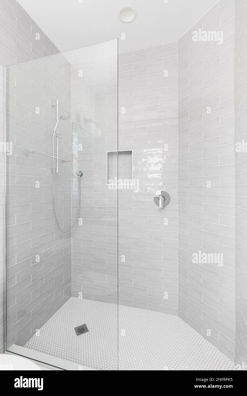 A walk-in shower with grey subway tiles, chrome shower head, and white ...