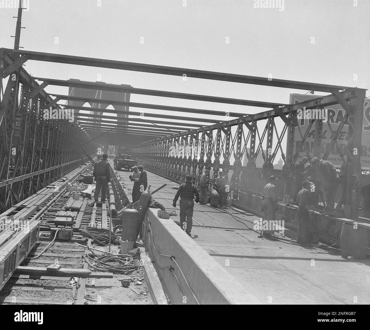 A crew of workmen are shown on the south roadway of the Brooklyn Bridge ...