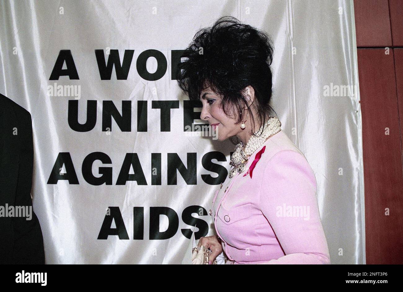 Actress Elizabeth Taylor walks by a poster which reads"A World United ...