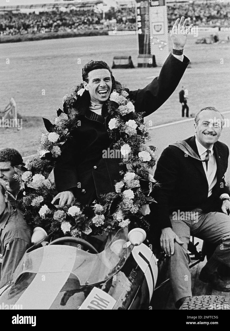 Wearing laurel wreath, Jim Clark waves from his Lotus as he makes a lap ...
