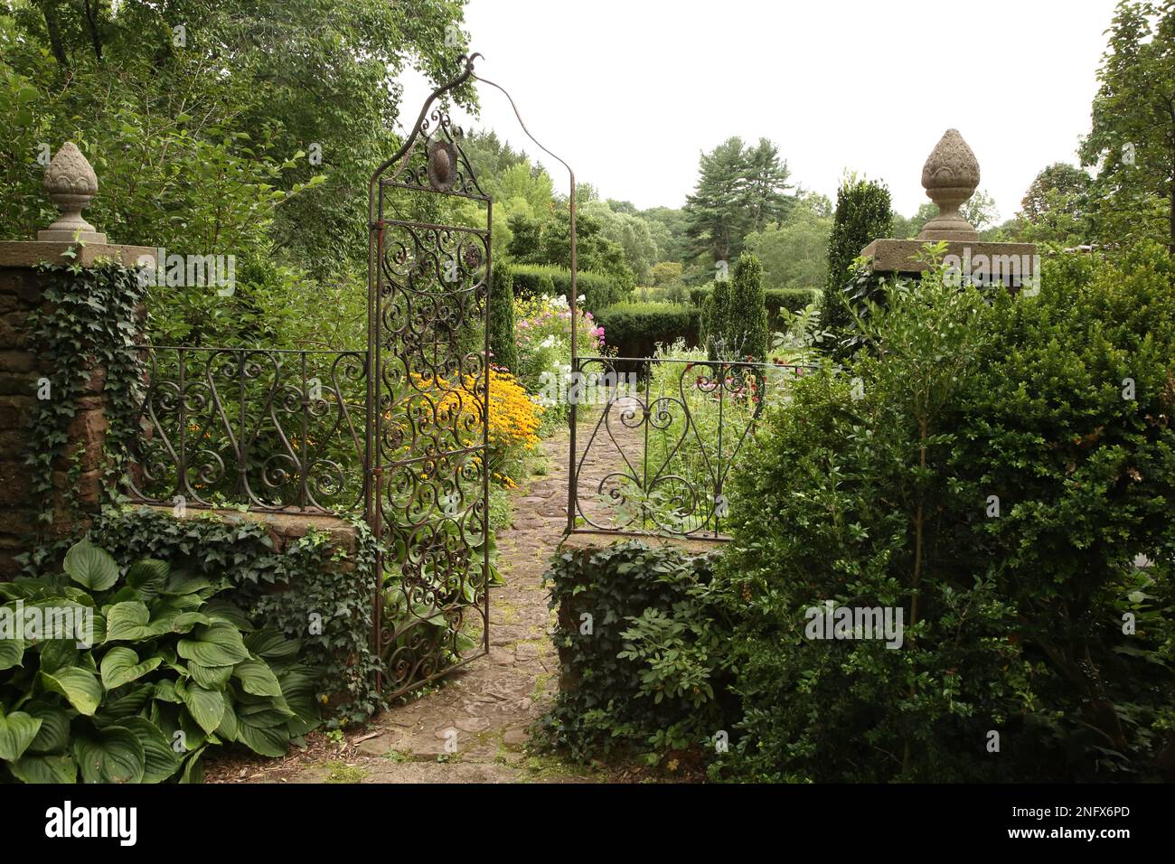 Willowwood Cottage Garden. Arrangements of flowering plants with grass pathways, Stone wall with ...