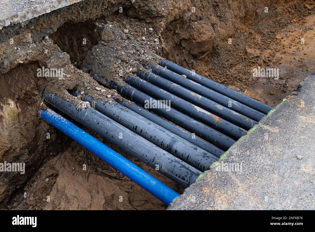 Plastic and metal pipes running across a trench dug in the ground. View ...