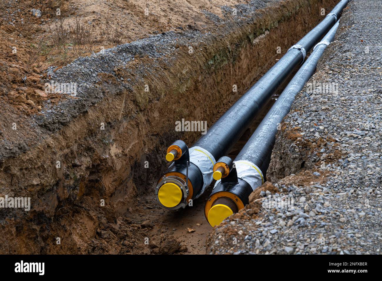 Large black metal pipes with a plastic sheath laid in a trench. Modern ...