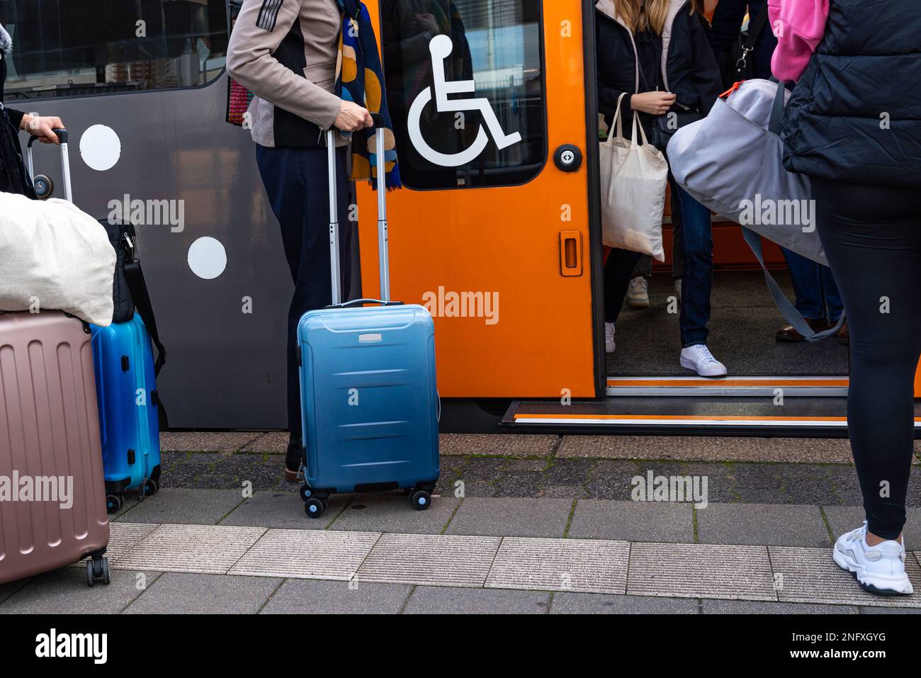 Passengers with trolleys entering and exiting the open doors of a ...
