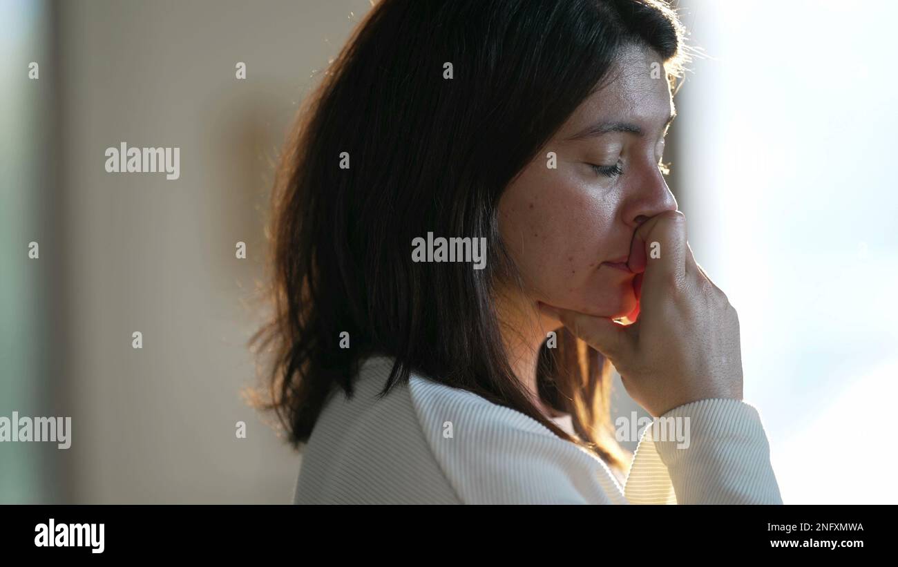 One worried woman standing by window with pensive preoccupied ...