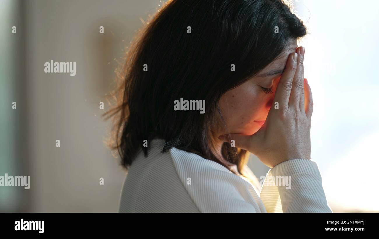 One worried woman standing by window with pensive preoccupied ...